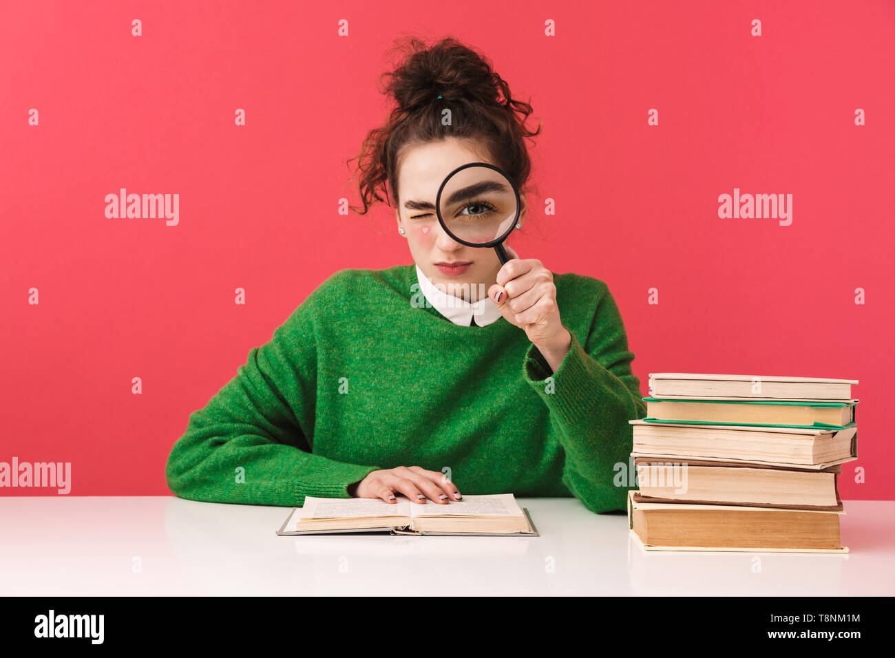 Beautiful young nerd student girl sitting at the table isolated over ...