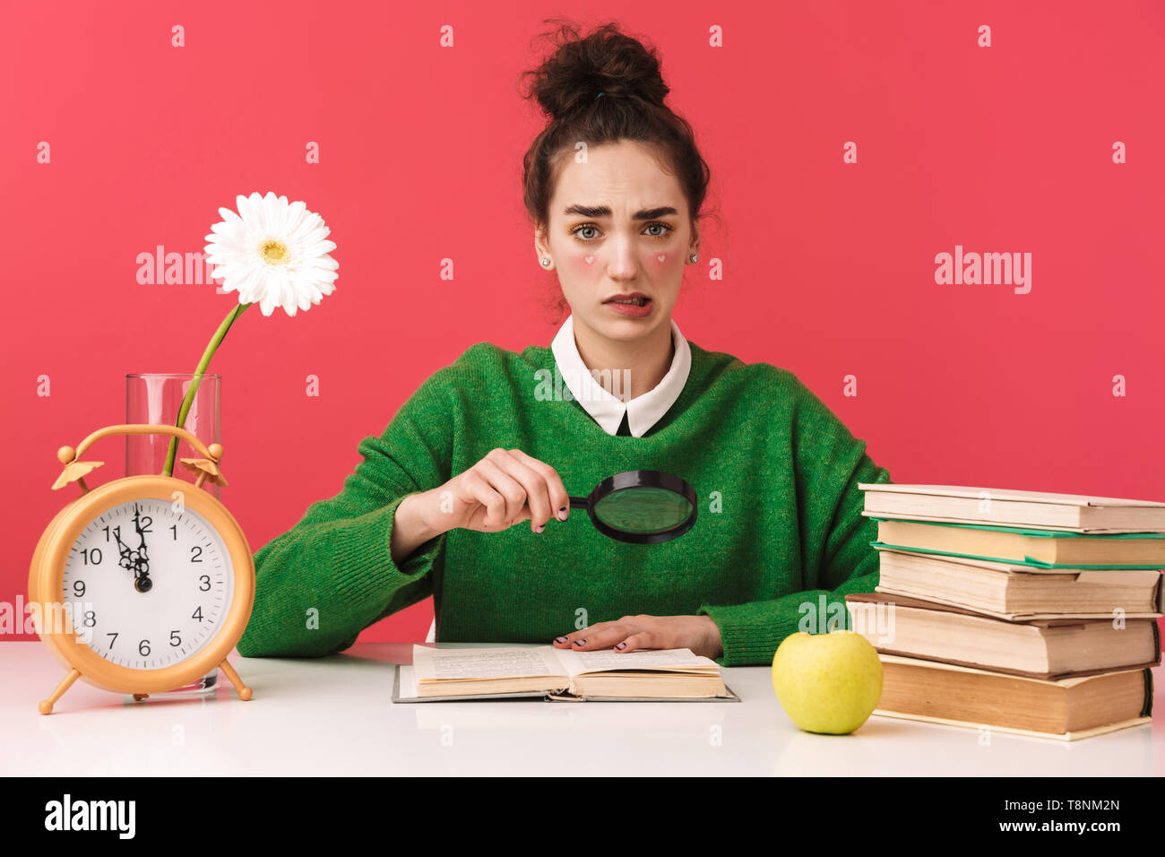 Beautiful young nerd student girl sitting at the table isolated over ...