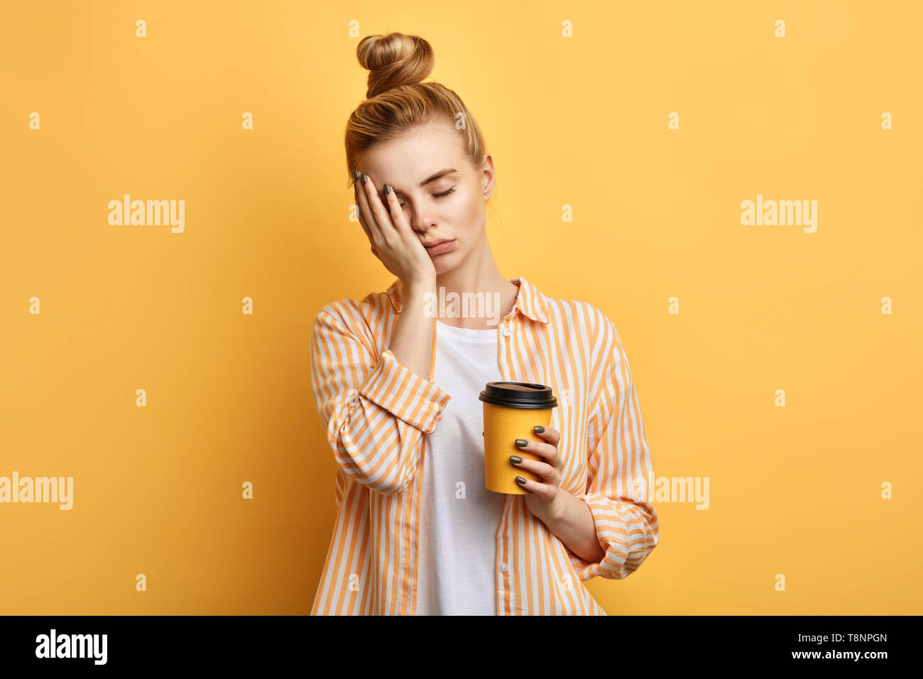 Tired sleepy woman holds a cup of coffee, has sad expression, closes ...