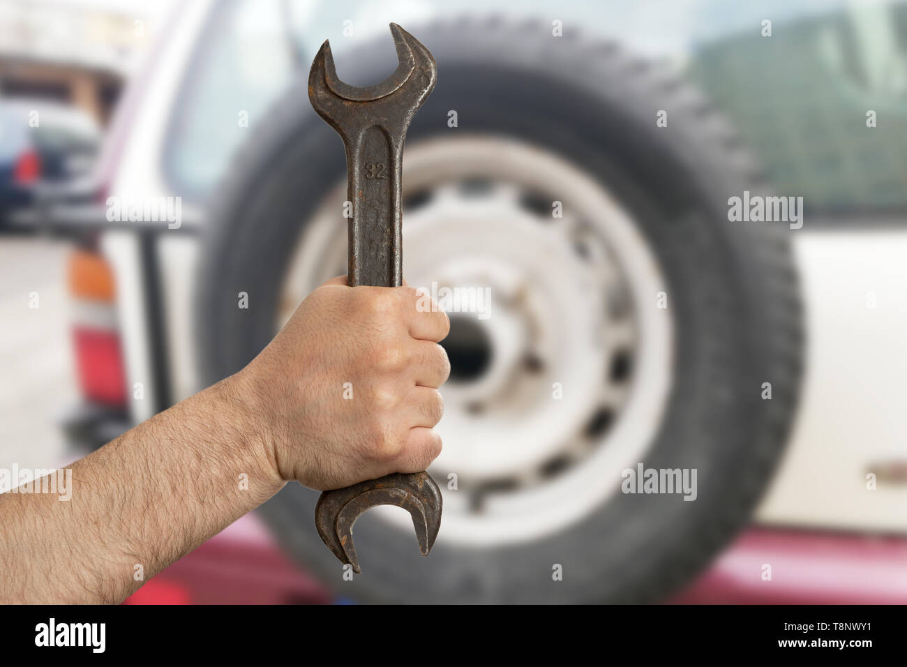 Man working as mechanic showing grey wrench with car tire in background ...