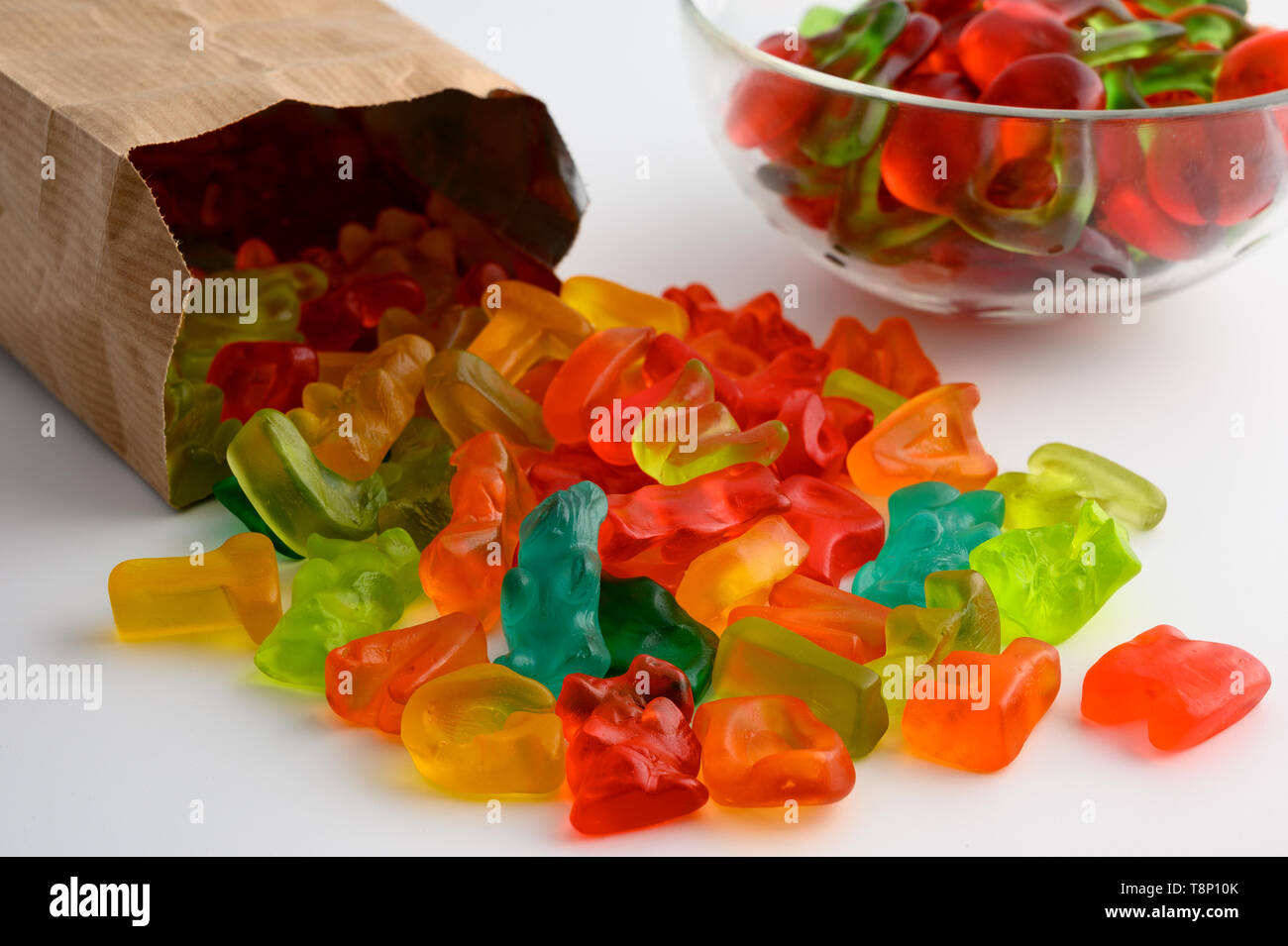 Glass bowls and paper bag of colorful gummy candies on white ...
