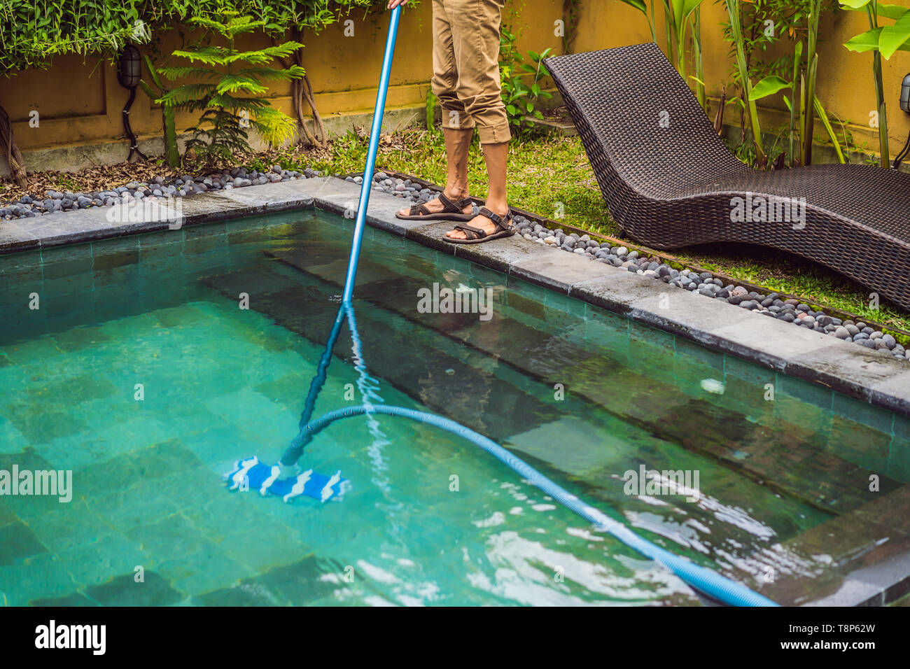 Cleaner of the swimming pool . Man in a blue shirt with cleaning ...