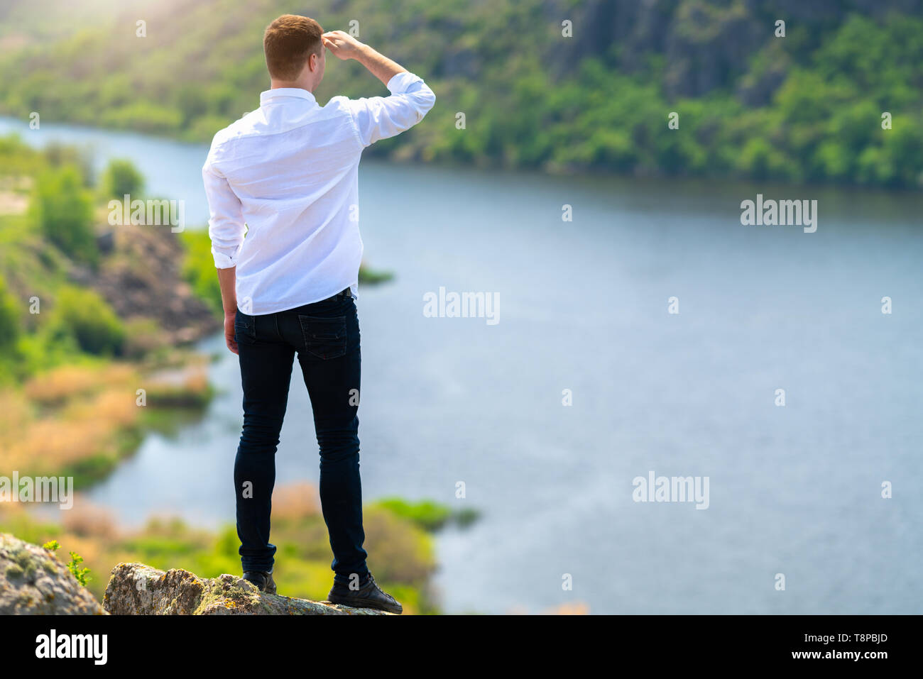 Man standing on a hilltop looking out over a river flowing through a ...