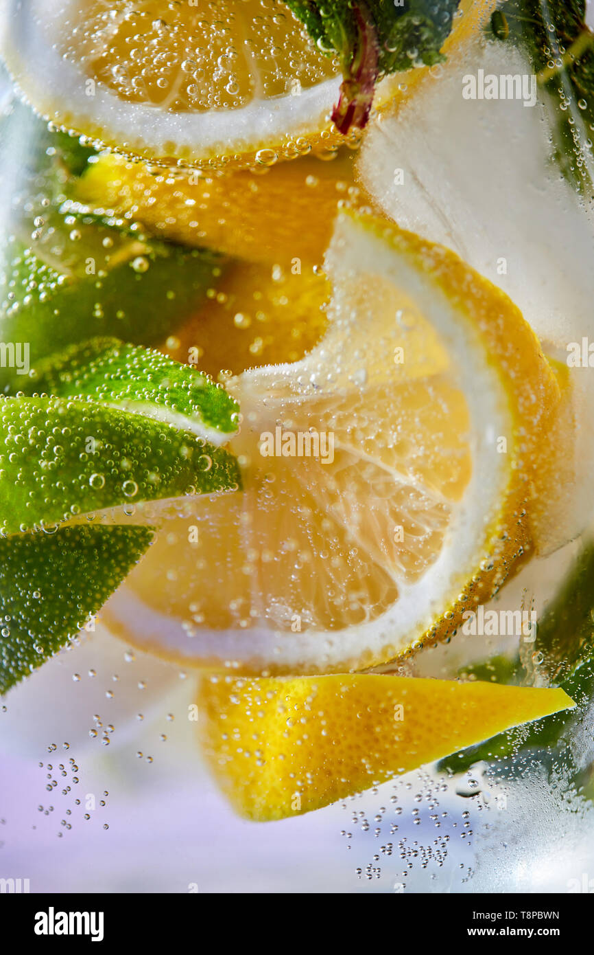 Slices of lemon and lime with bubbles of water in a glass. Macro photo of refreshing lemonade ...