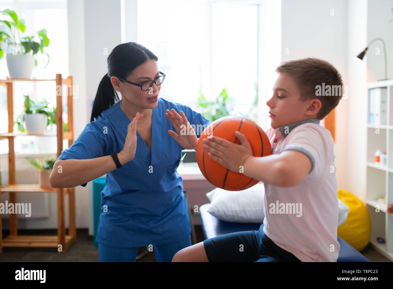 Active dark-haired nurse in blue uniform showing example Stock Photo ...