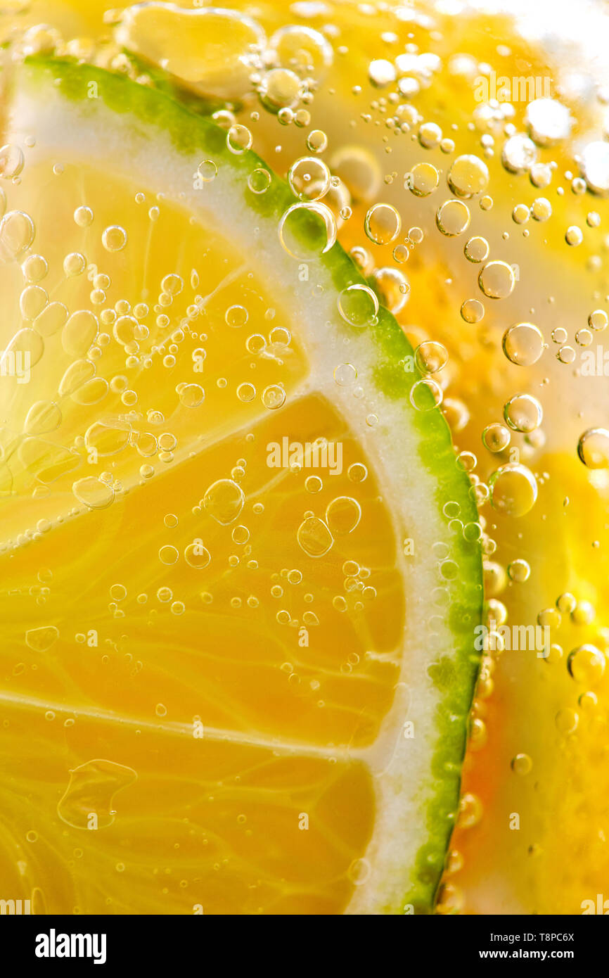 Juicy slices of ripe lemon and lime with bubbles in a glass of water ...