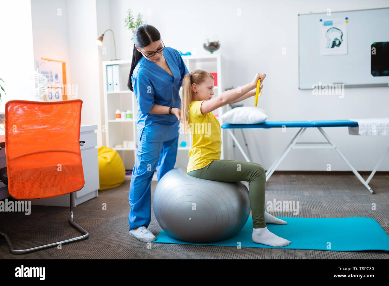 Concentrated long-haired therapist in blue uniform correcting posture ...