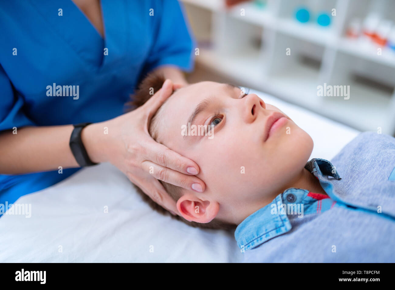 Tranquil short-haired boy calmly lying during relaxing head massage ...