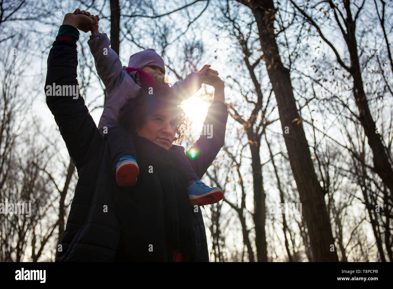 Young dad carrying baby on his shoulders in a forest holding her hands ...