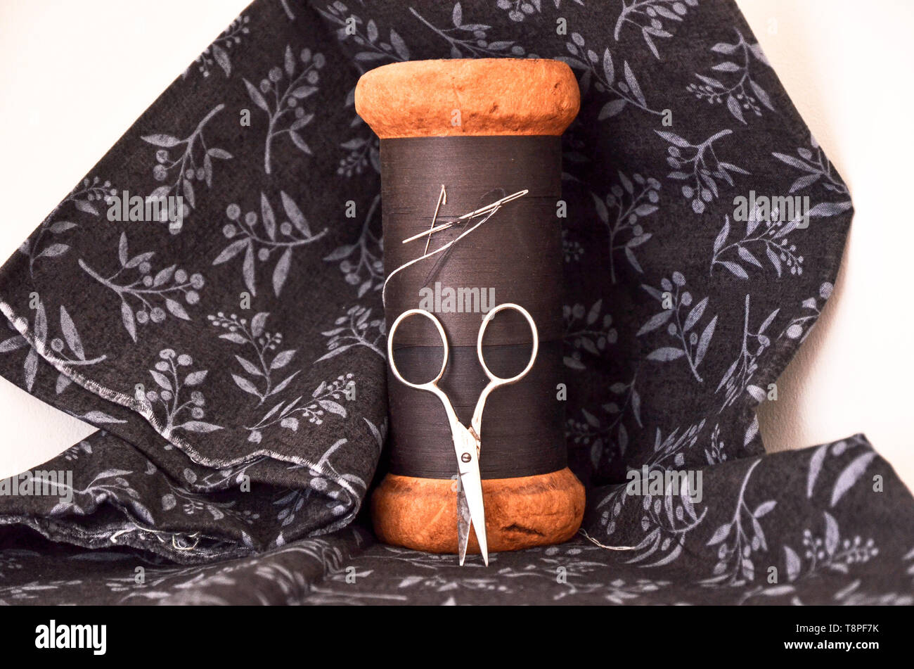 large antique spool of black thread with needles and scissors against a ...