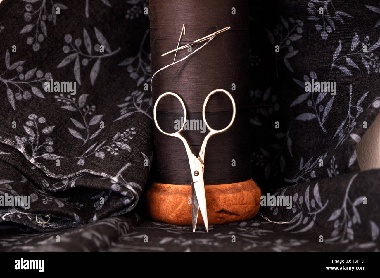 large antique spool of black thread with needles and scissors against a ...