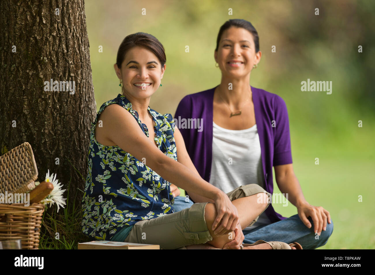 Two smiling friends enjoying a picnic under a tree Stock Photo - Alamy