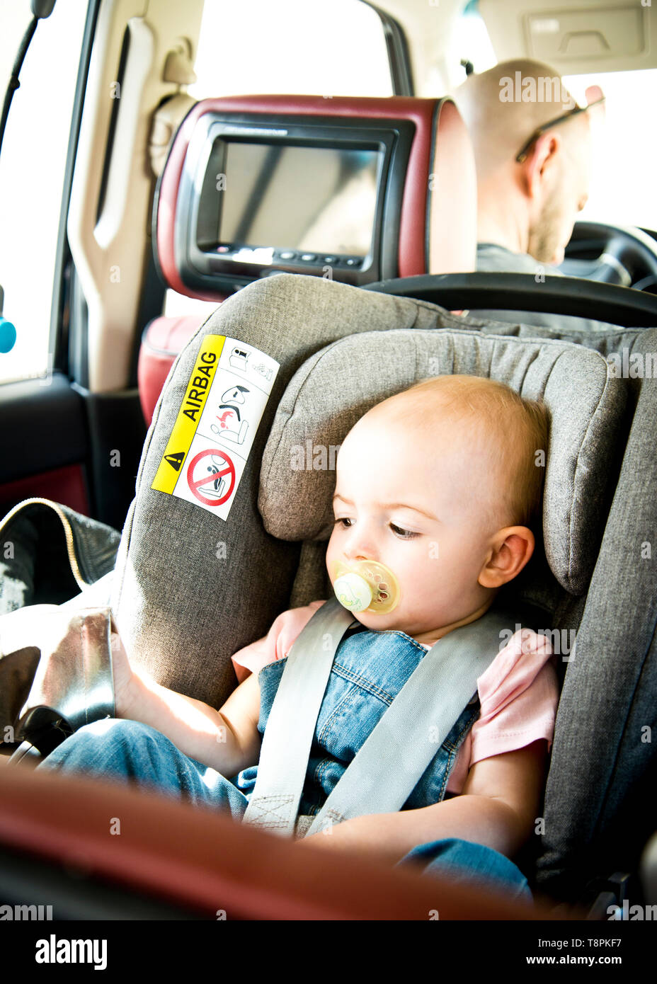 young baby girl with pacifier in her mouth, sitting in car seat, secure ...
