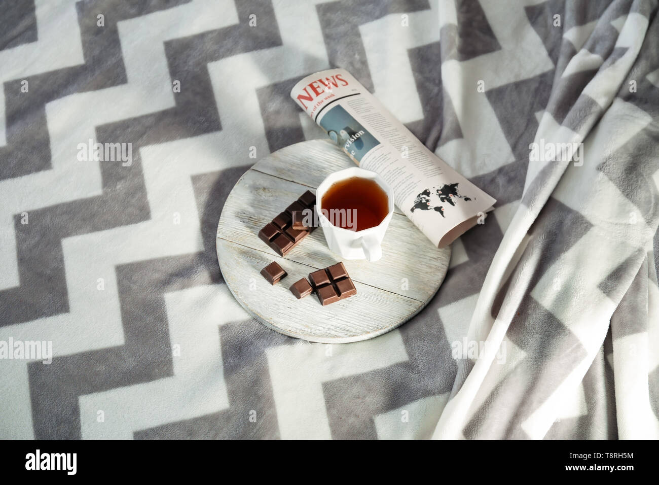 Wooden board with chocolate, newspaper and cup of tea on bed Stock ...