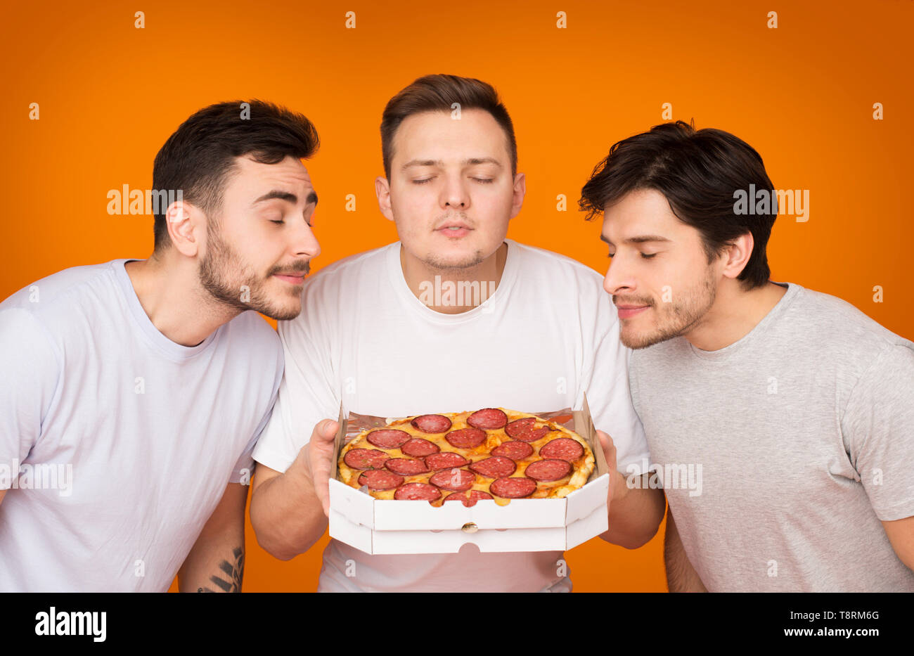 Three Men Smelling Hot Pizza Over Orange Background Stock Photo - Alamy