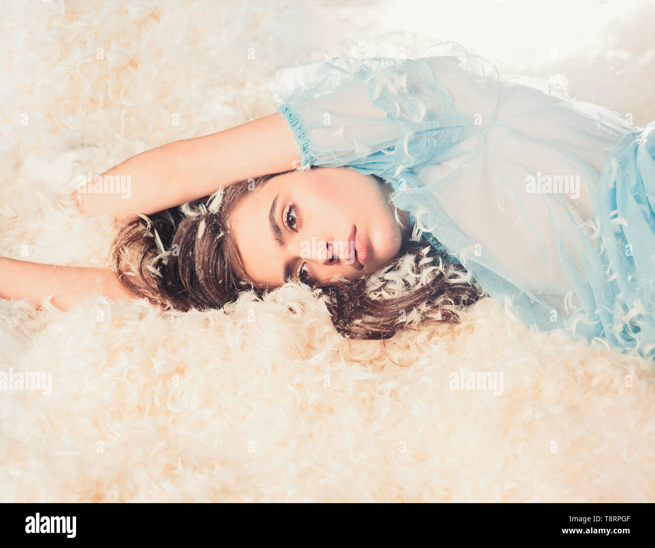 Girl on calm face lay on bed covered with feathers and fluff. Airiness ...
