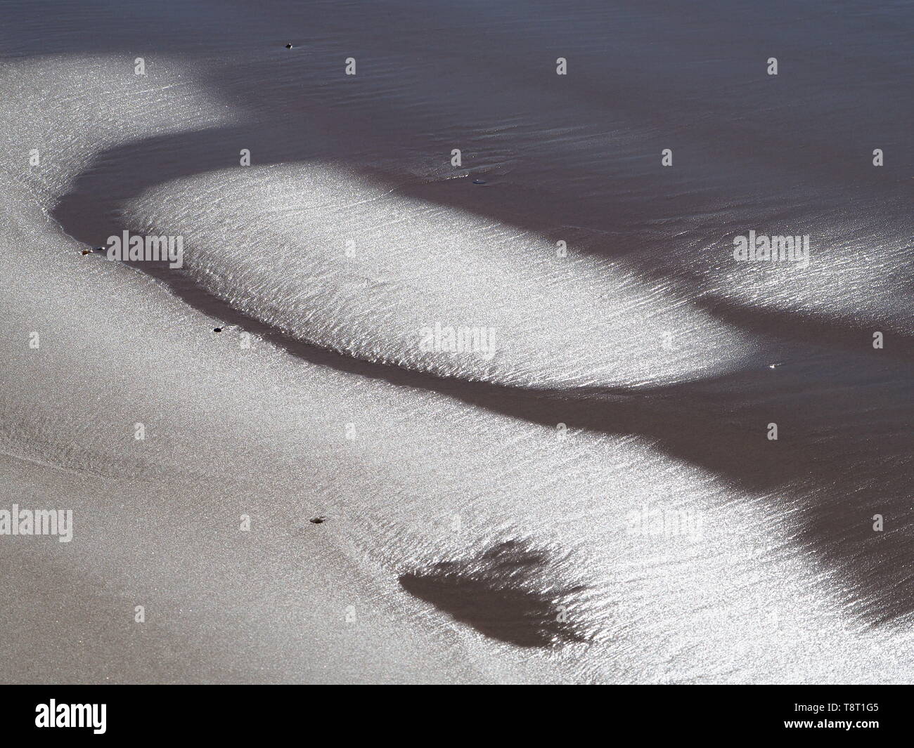 Patterns formed by water, sunlight and shadow on the wet shiny sand at ...
