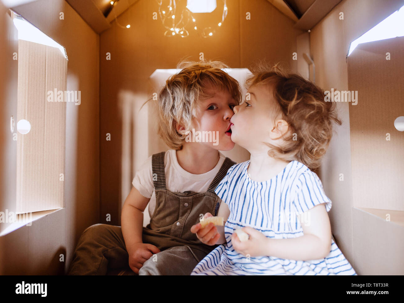 Two happy toddler children playing indoors in cardboard house at home ...
