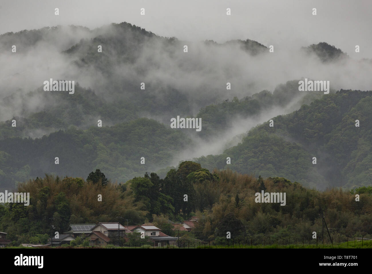 Mist rises from rugged mountain over cluster of Japanese houses Stock ...