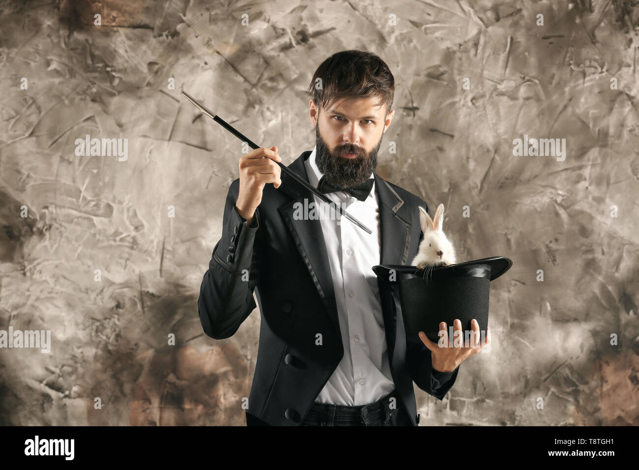 Magician holding hat with rabbit on grunge background Stock Photo - Alamy