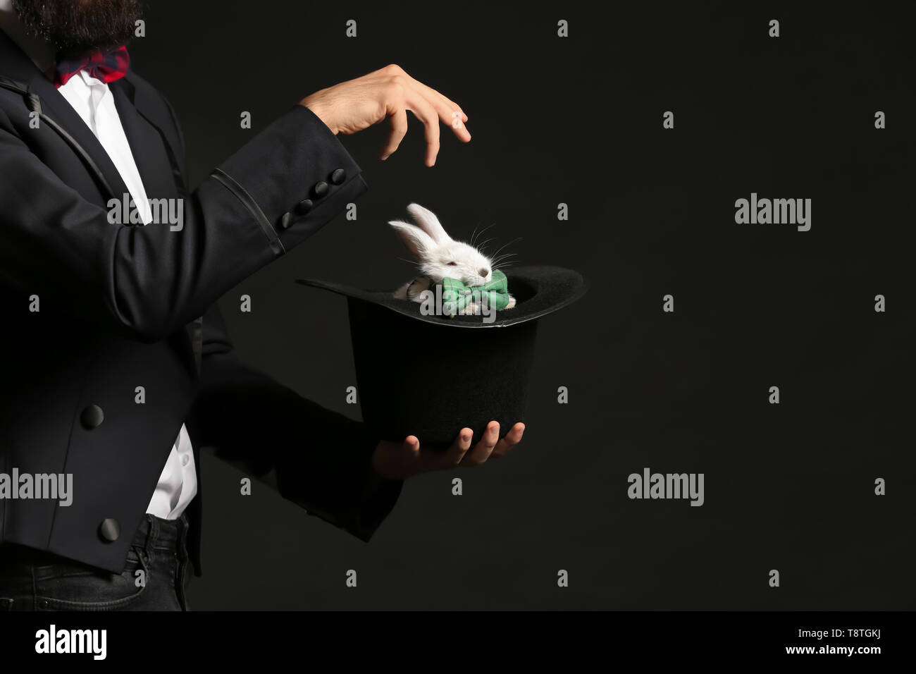 Magician holding hat with rabbit on dark background Stock Photo - Alamy