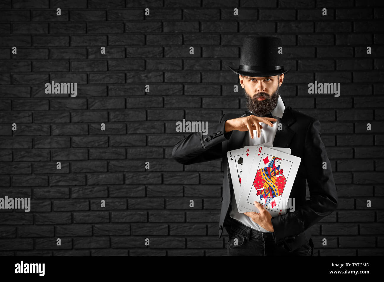 Magician with cards against dark brick wall Stock Photo - Alamy