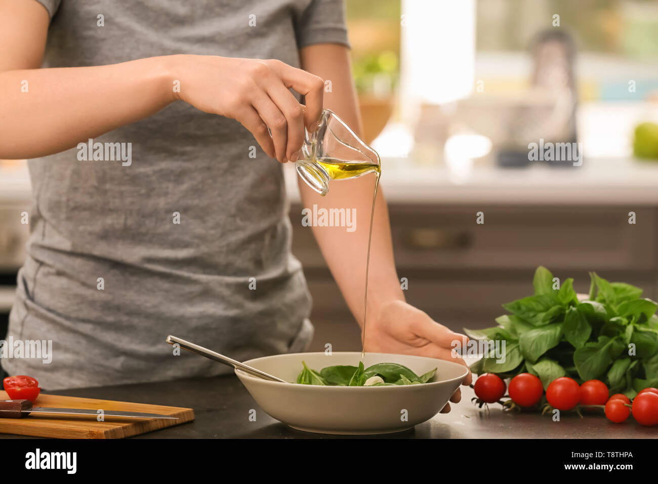 Woman pouring oil onto fresh salad with basil at table Stock Photo - Alamy