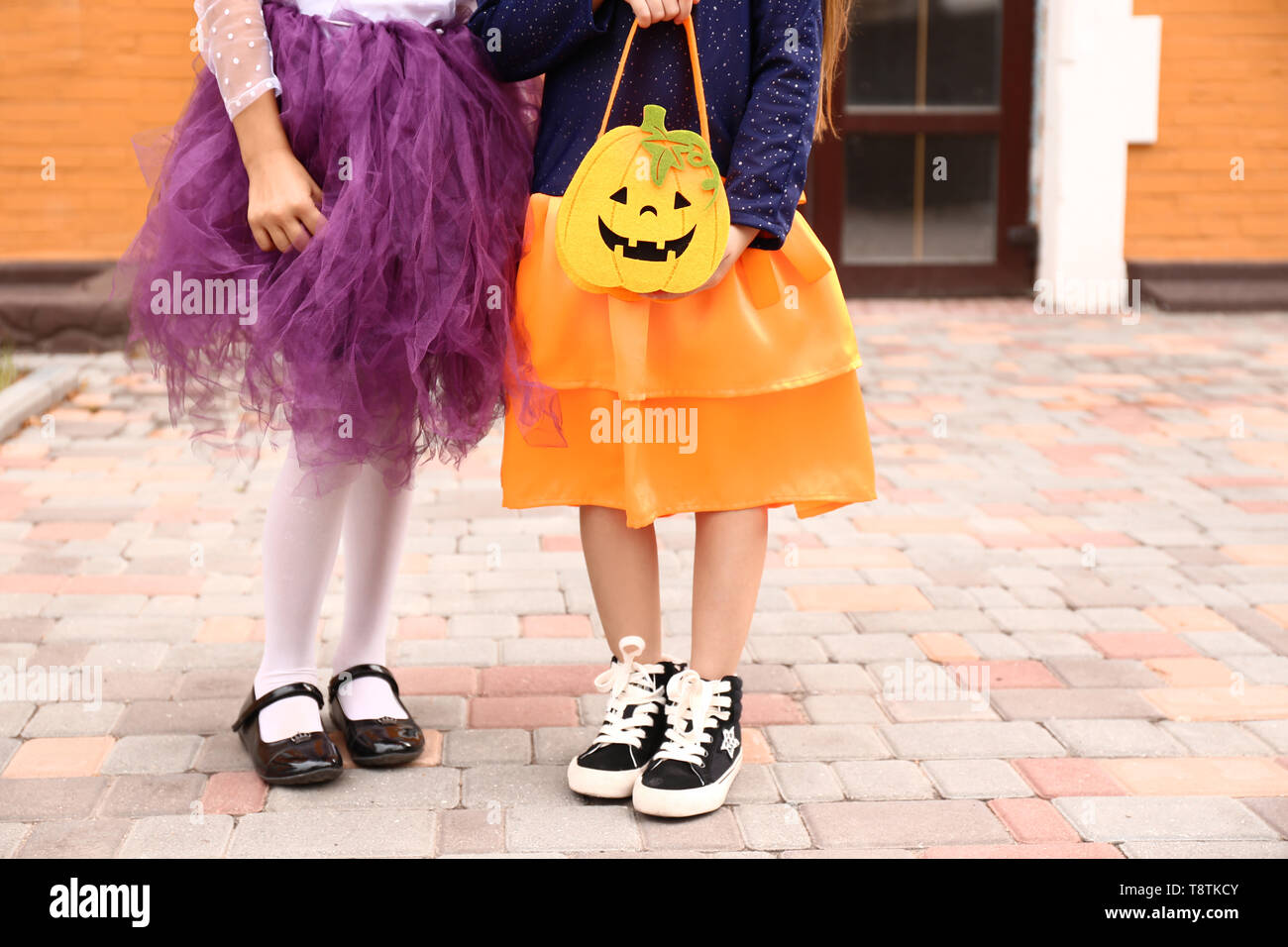 Cute little girls in Halloween costumes trick-or-treating outdoors ...