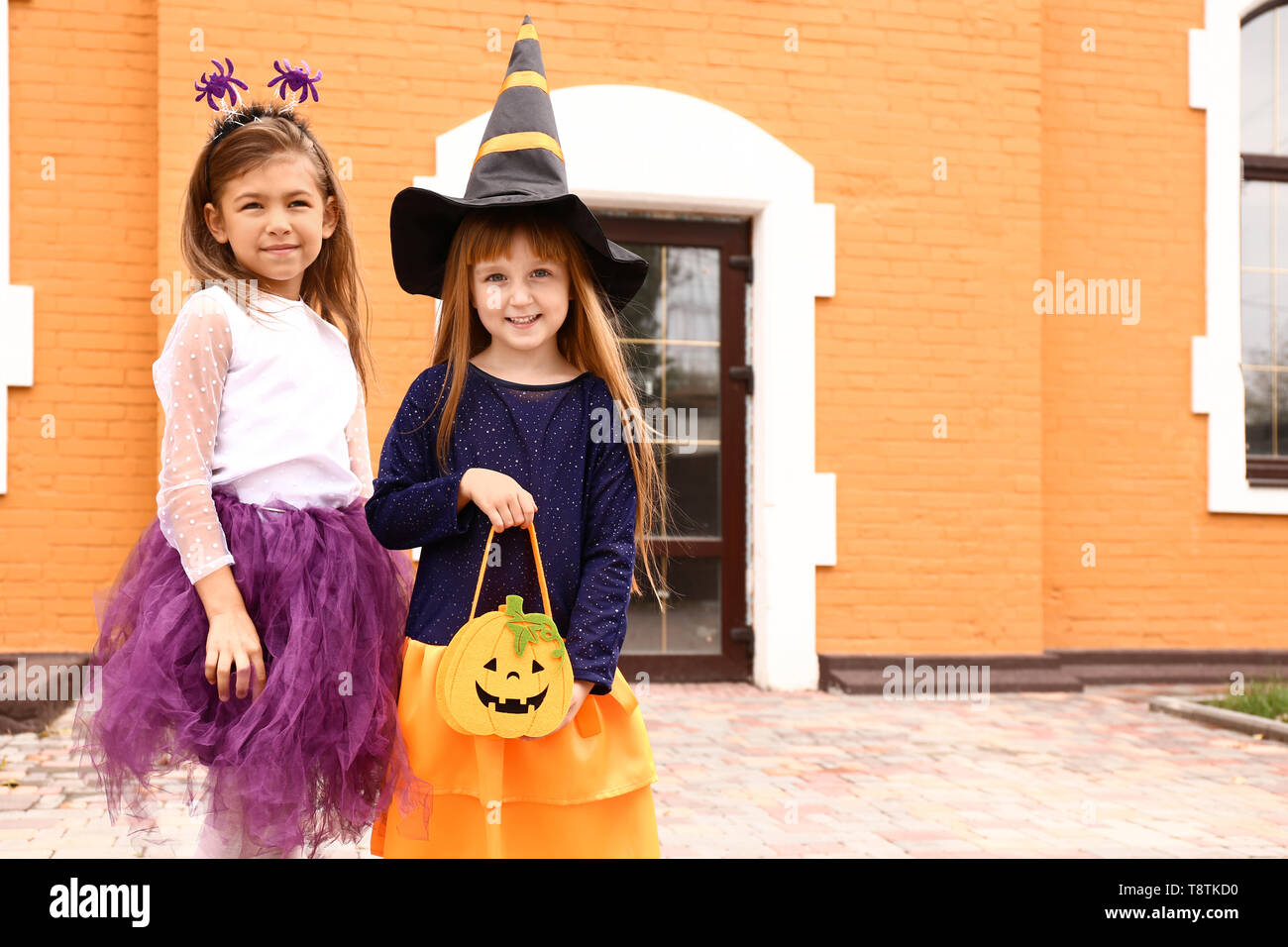 Cute little girls in Halloween costumes trick-or-treating outdoors ...