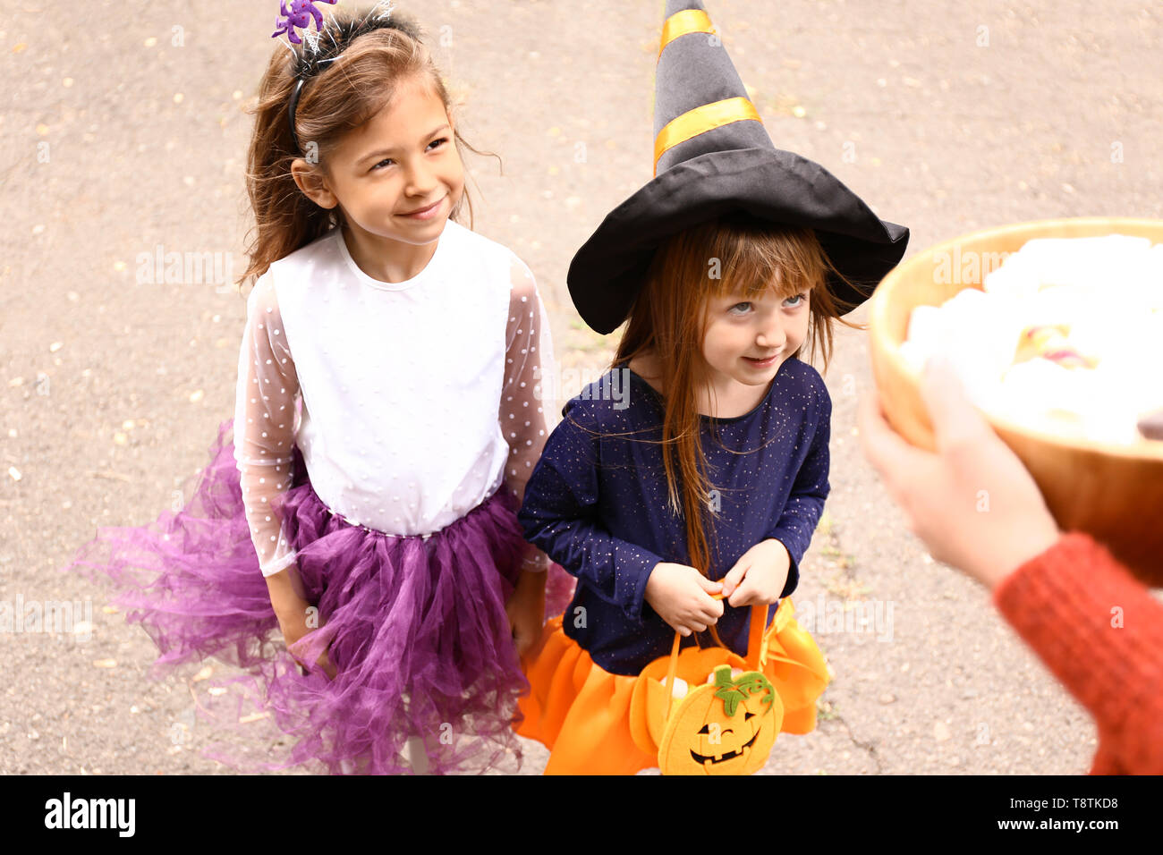 Cute little girls in Halloween costumes trick-or-treating outdoors ...