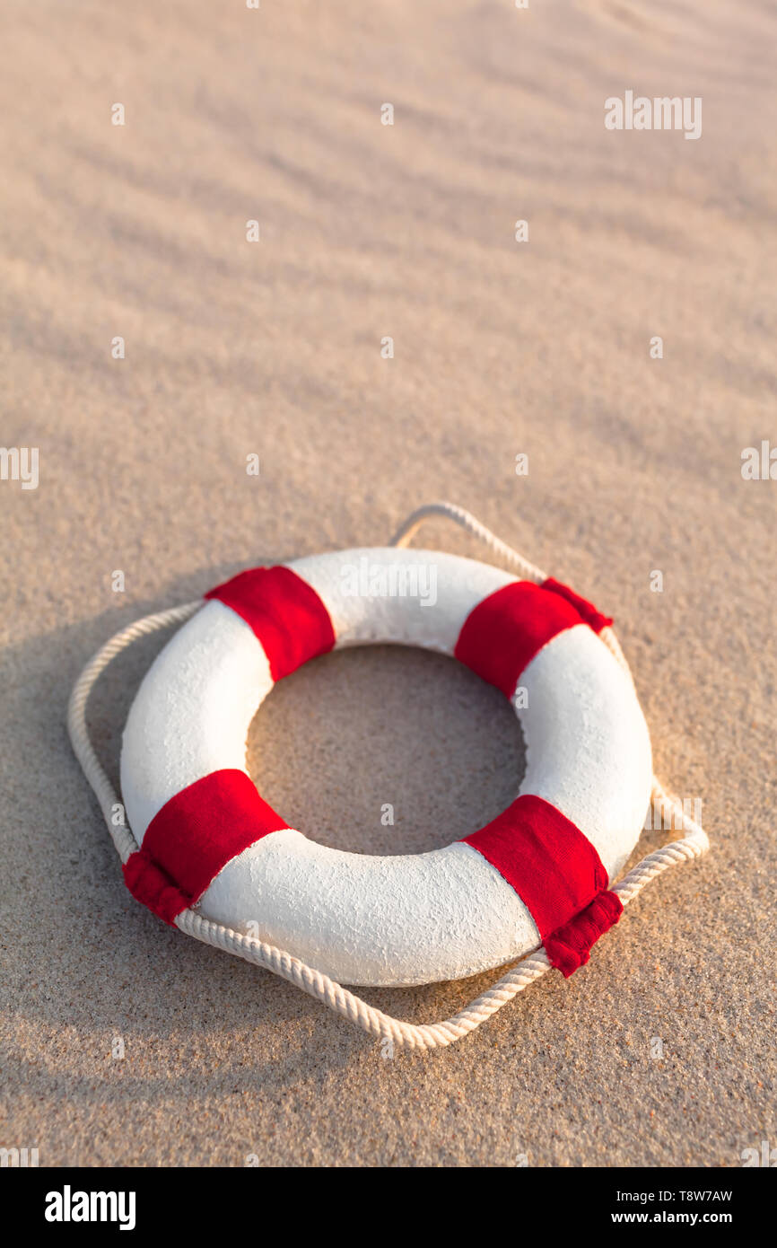 Nostalgic miniature life buoy with rope and red stripes on wavy beach ...