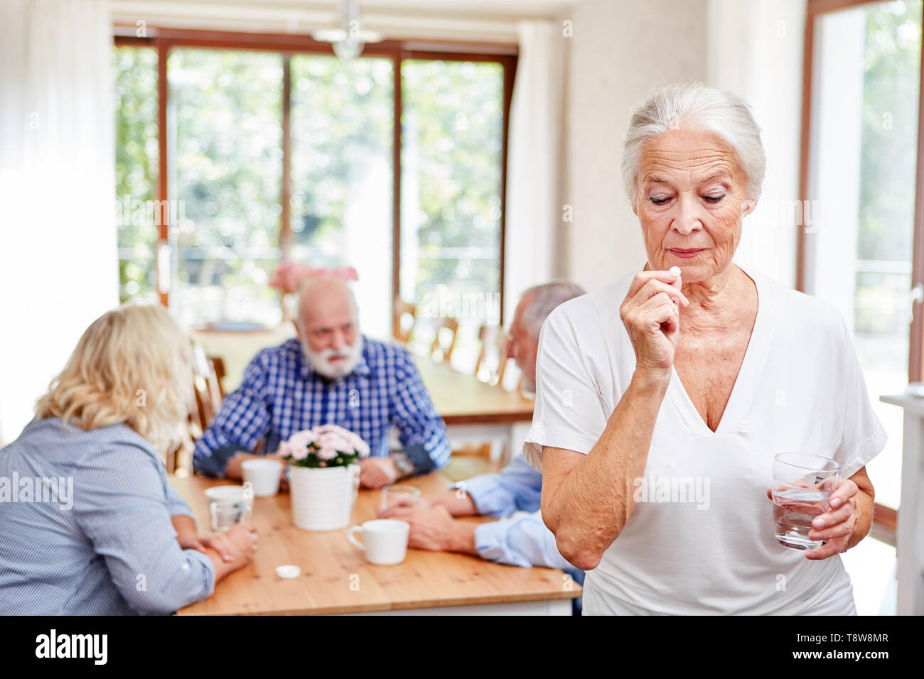 Sick senior woman in retirement home takes a tablet with a glass of ...