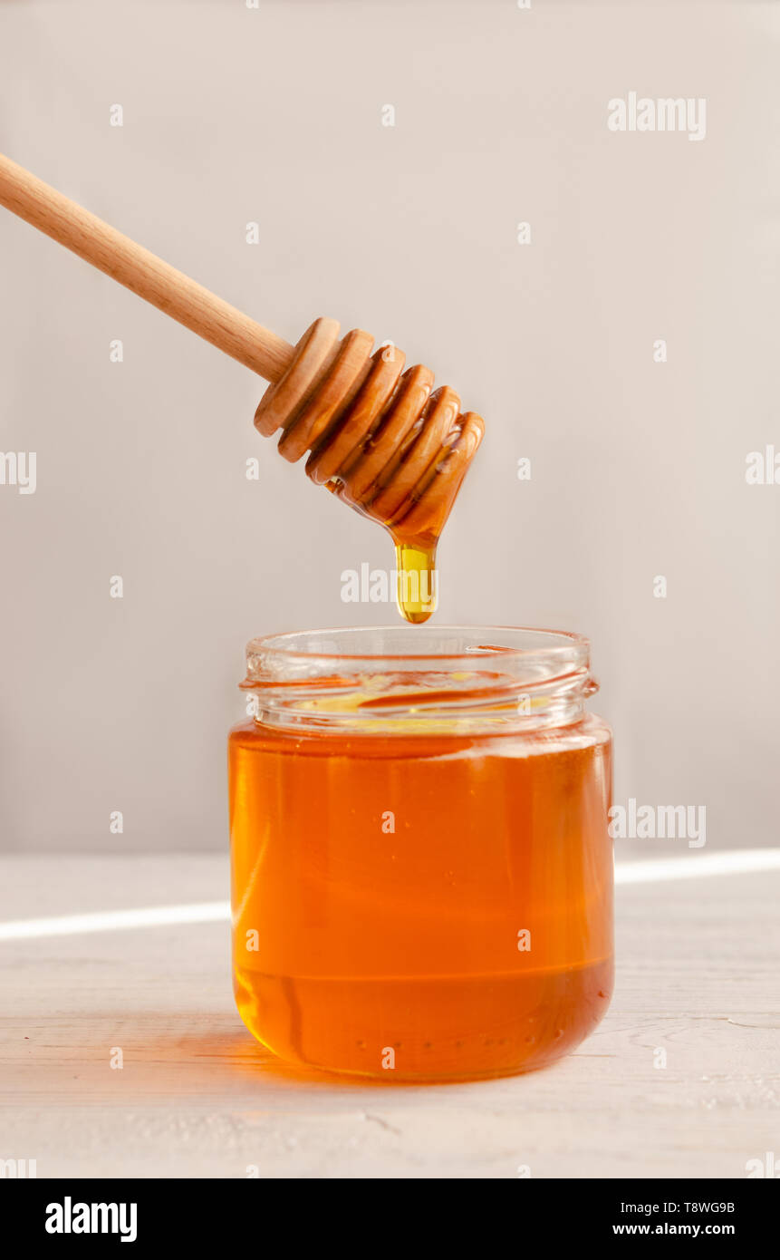 A viscous stream of sweet amber flower honey flows from a wooden honey ...