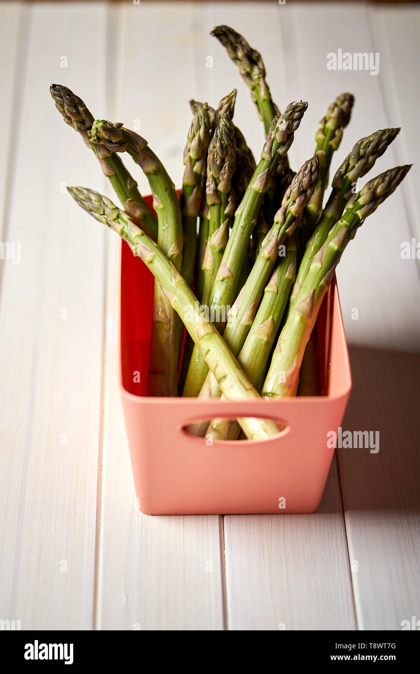 Fresh asparagus in coral container on white kitchen table Stock Photo ...