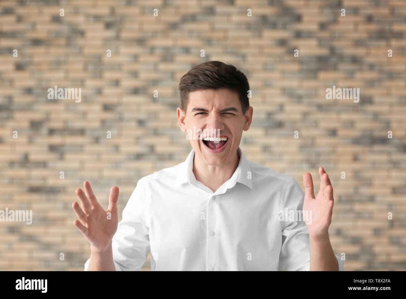 Portrait of aggressive young man against brick wall Stock Photo - Alamy