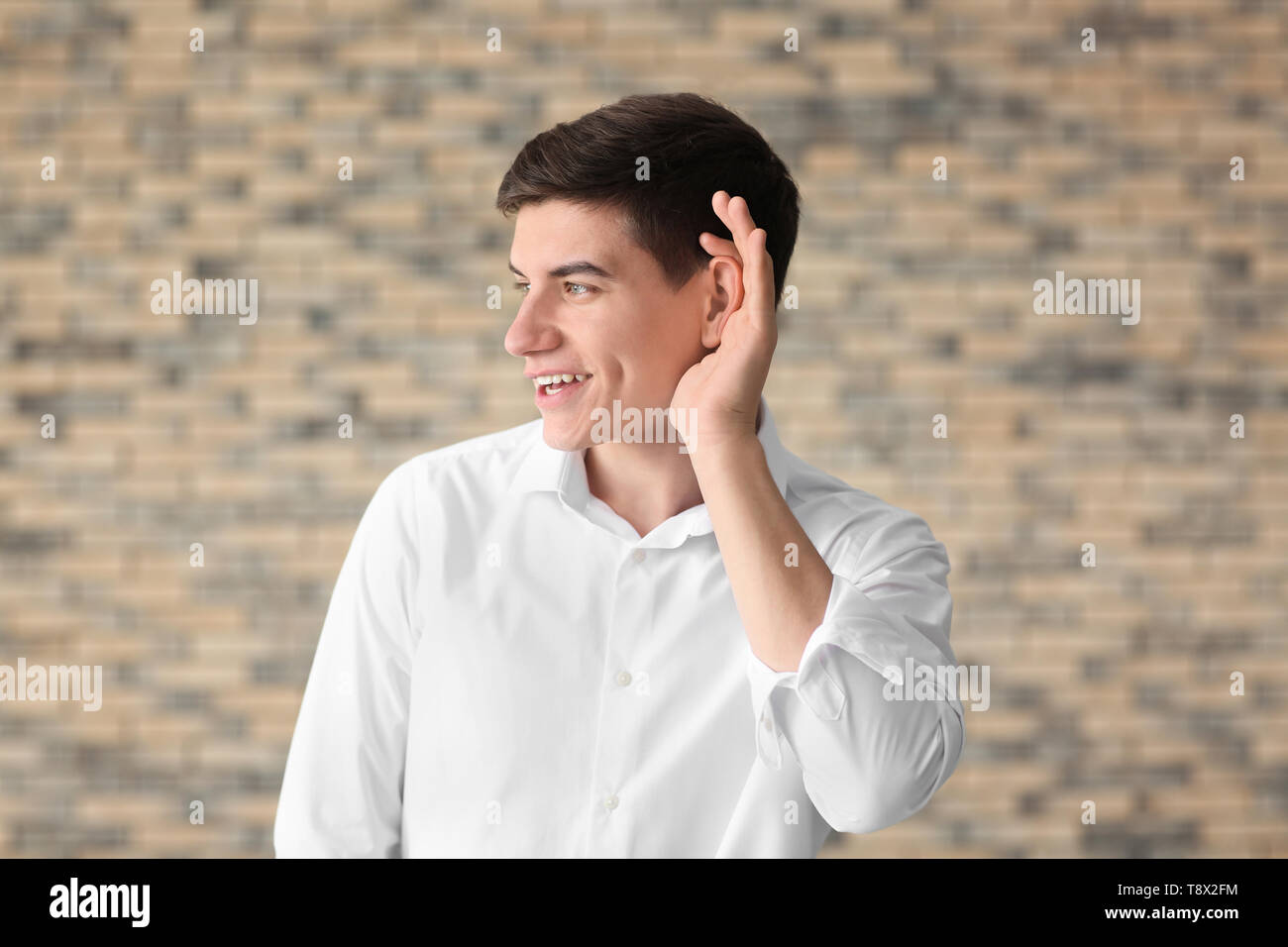 Portrait of handsome young man listening to someone against brick wall ...