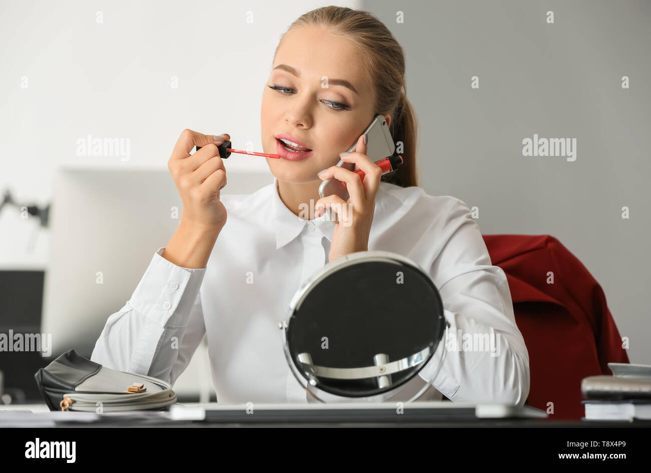Beautiful female secretary applying makeup while talking on mobile ...