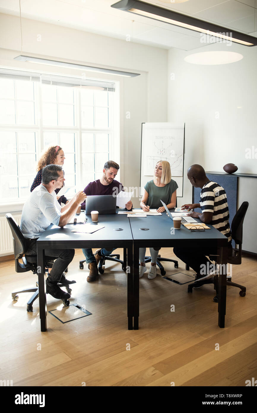 Diverse group of young designers discussing work together while sitting ...