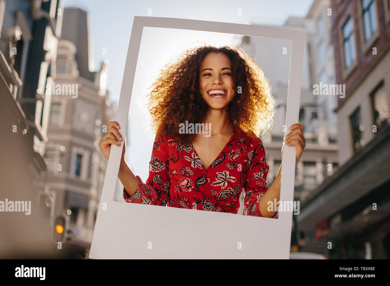 Excited girl with empty photo frame standing outdoors in the city ...