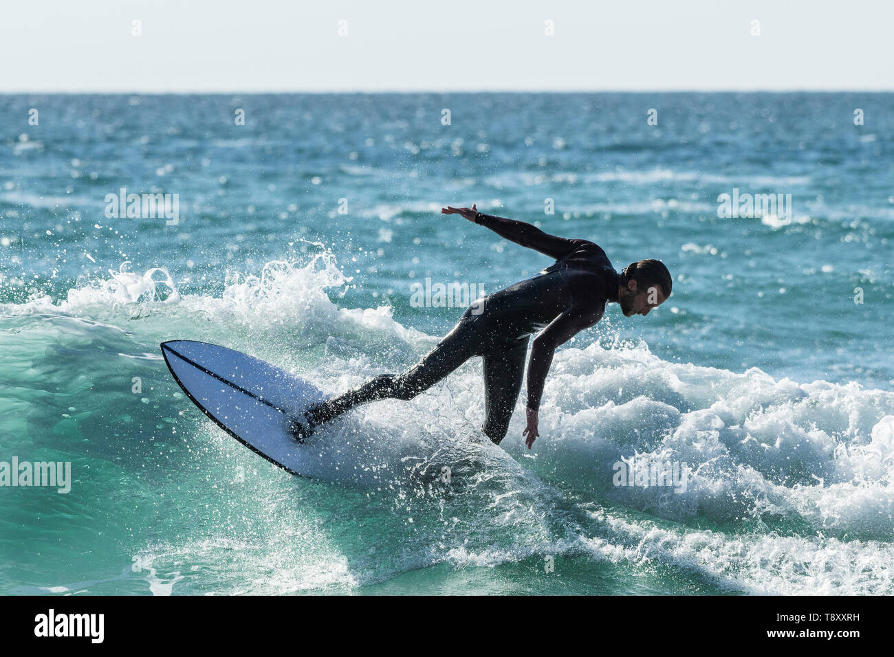 Surfing action as a surfer rides a wave in a jade coloured sea at ...