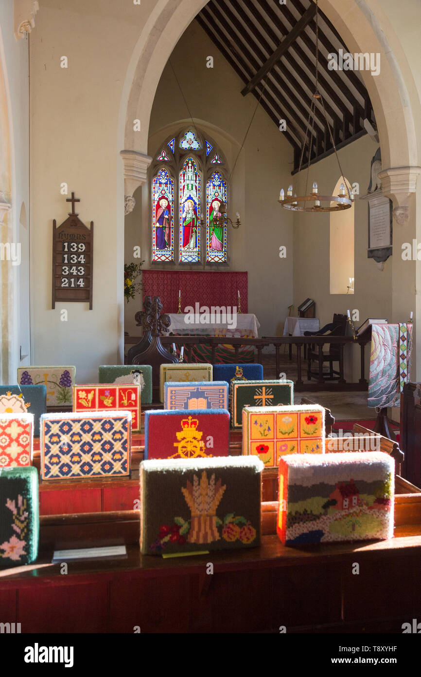 Knitted woollen pew kneelers rest on wooden pews, view towards altar ...