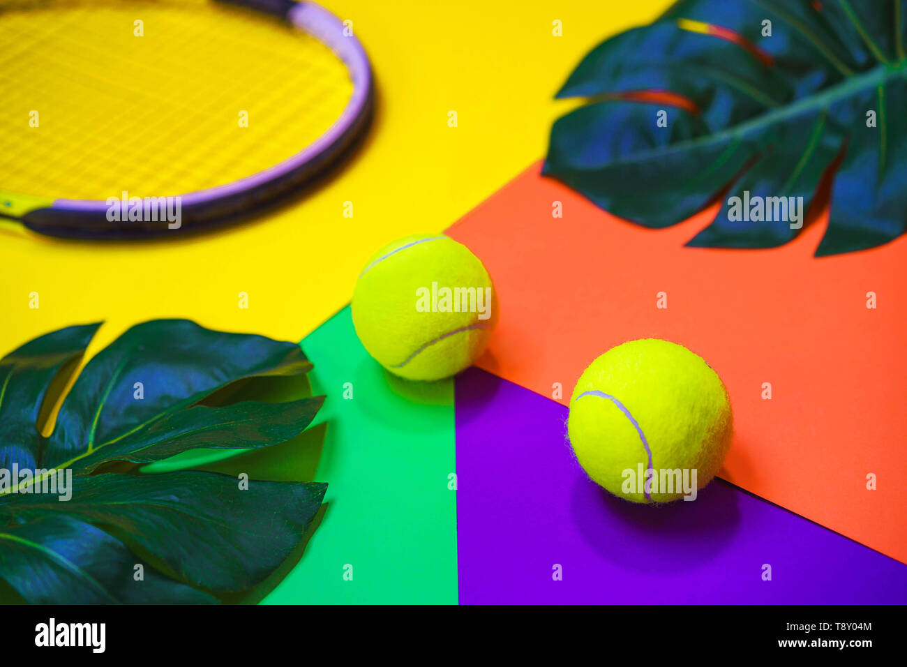 Tennis layout with tennis balls, racket and tropical monstera leaves on ...