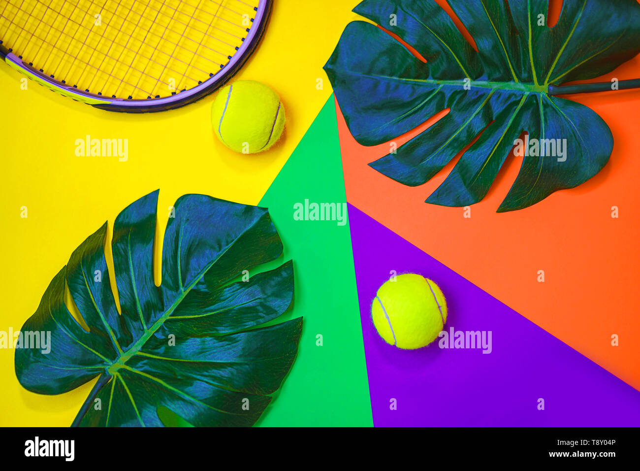 Tennis layout with tennis balls, racket and tropical monstera leaves on ...