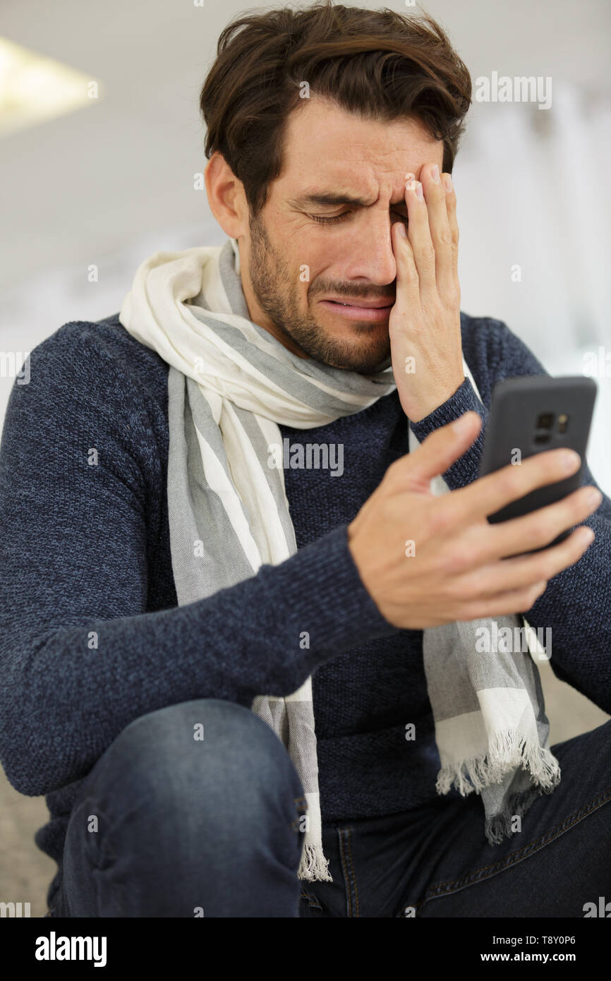crying young man looking at his smartphone Stock Photo - Alamy