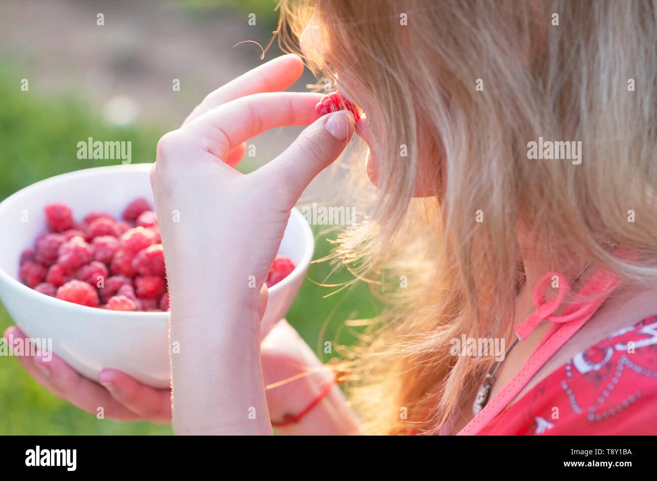 Young girl holding a plate of raspberries, sitting on green grass ...