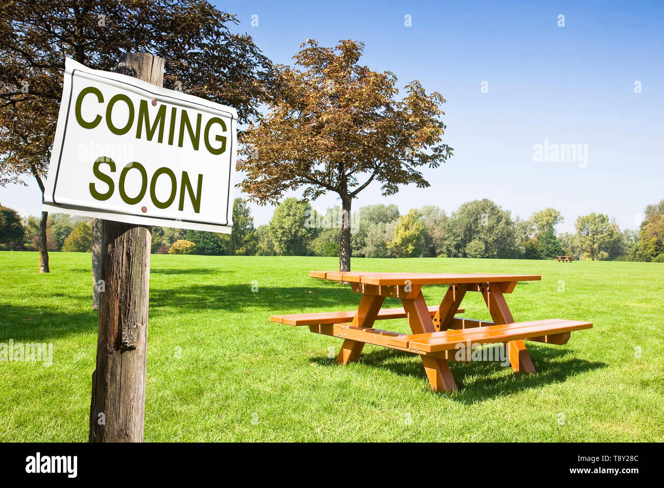 Coming soon written on a signboard near a picnic table on a green ...