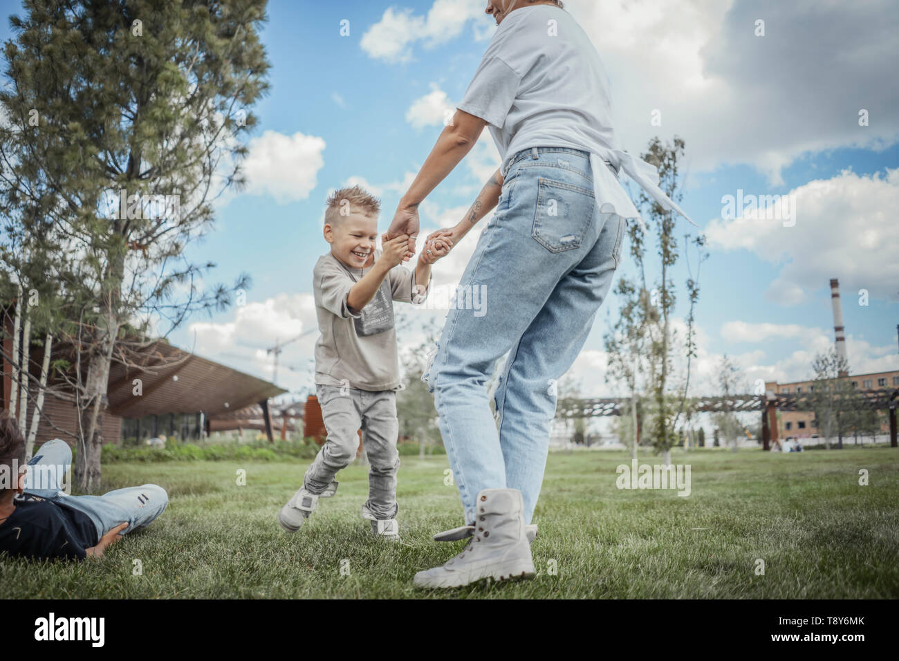 Pretty mum turning around, whirling with her son at park. Happy family ...
