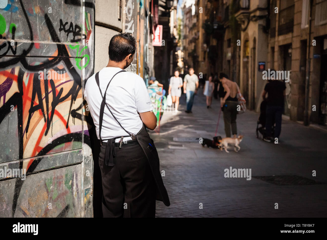 Man with apron standing in the street of Raval quarter of Barcelona ...
