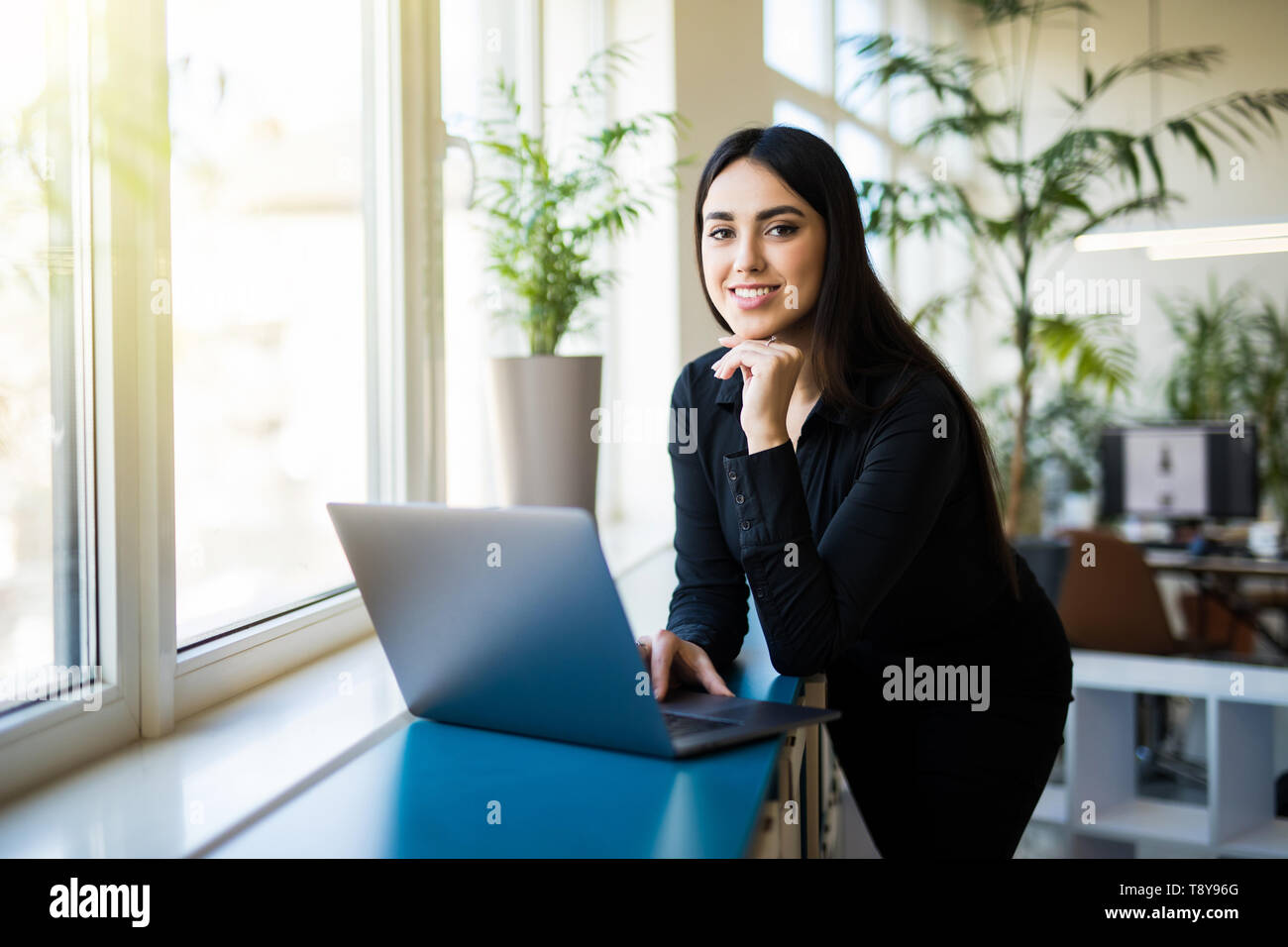 Beautiful business woman is using a laptop and smiling while working in ...