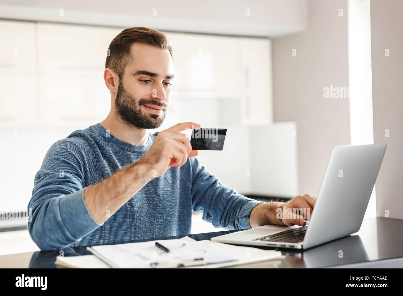 Happy handsome man freelancer sitting at the kitchen table, working on ...